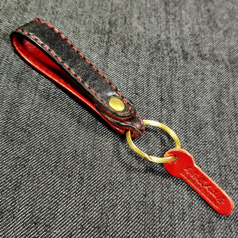 専門の馬具職人がハンドメイド、総手縫いで仕上げましたキーホルダーです。表側を黒革、裏側を赤革を使用し、赤糸で縫いあげました。金具部分全ては真鍮製を使用しております。画像が現物になります。革の状態など、画像にてご判断ください。受注生産品ではあ...