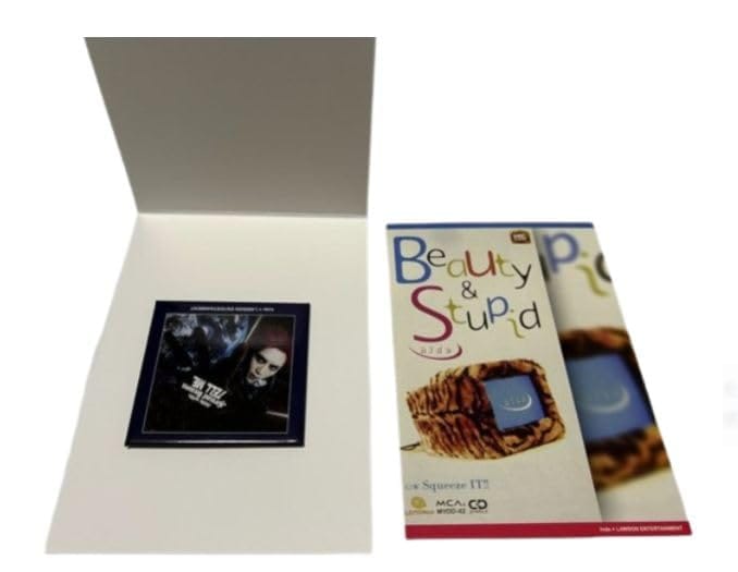 hide 2026くじD賞の缶バッジ＆ポストカードAセット、缶バッジは「TELL ME 2000」ビジュアル、ポストカードは「Beauty & Stupid」デザインで、ポストカード面には「Beauty & Stupid」「hide」「 L...