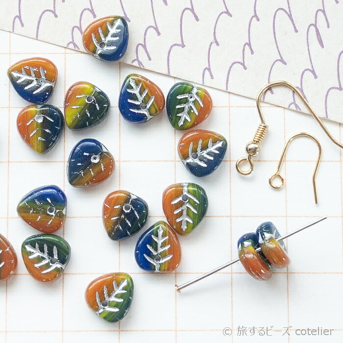 小ぶりのリーフ型のプレスビーズ。チェコ製のガラスビーズです。 【サイズ】 9 ミリ (画像のマス目は1センチ四方です) 【個数】 18個 【色味】不透明オレンジ、ブルー、イエロー系ストライプにシルバー系コーティング 【色違い】cotelie...