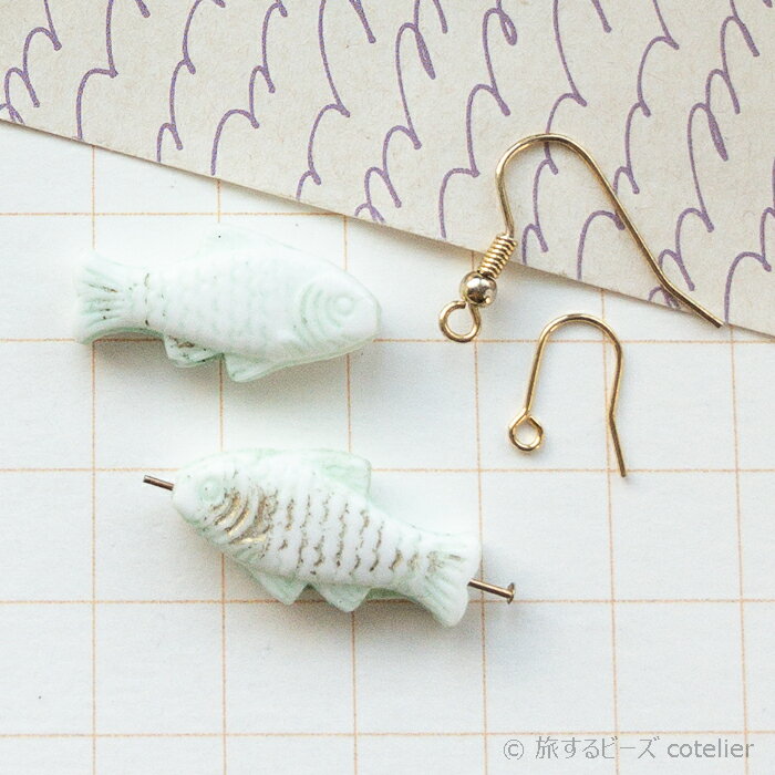 リアルな雰囲気の魚型のプレスビーズ。チェコ製のガラスビーズです。 【サイズ】 10x24ミリ (画像のマス目は1センチ四方です) 【個数】2個 【色味】不透明ホワイトにグリーン系コーティング、片面のみゴールド系コーティング※色味には個体差が...