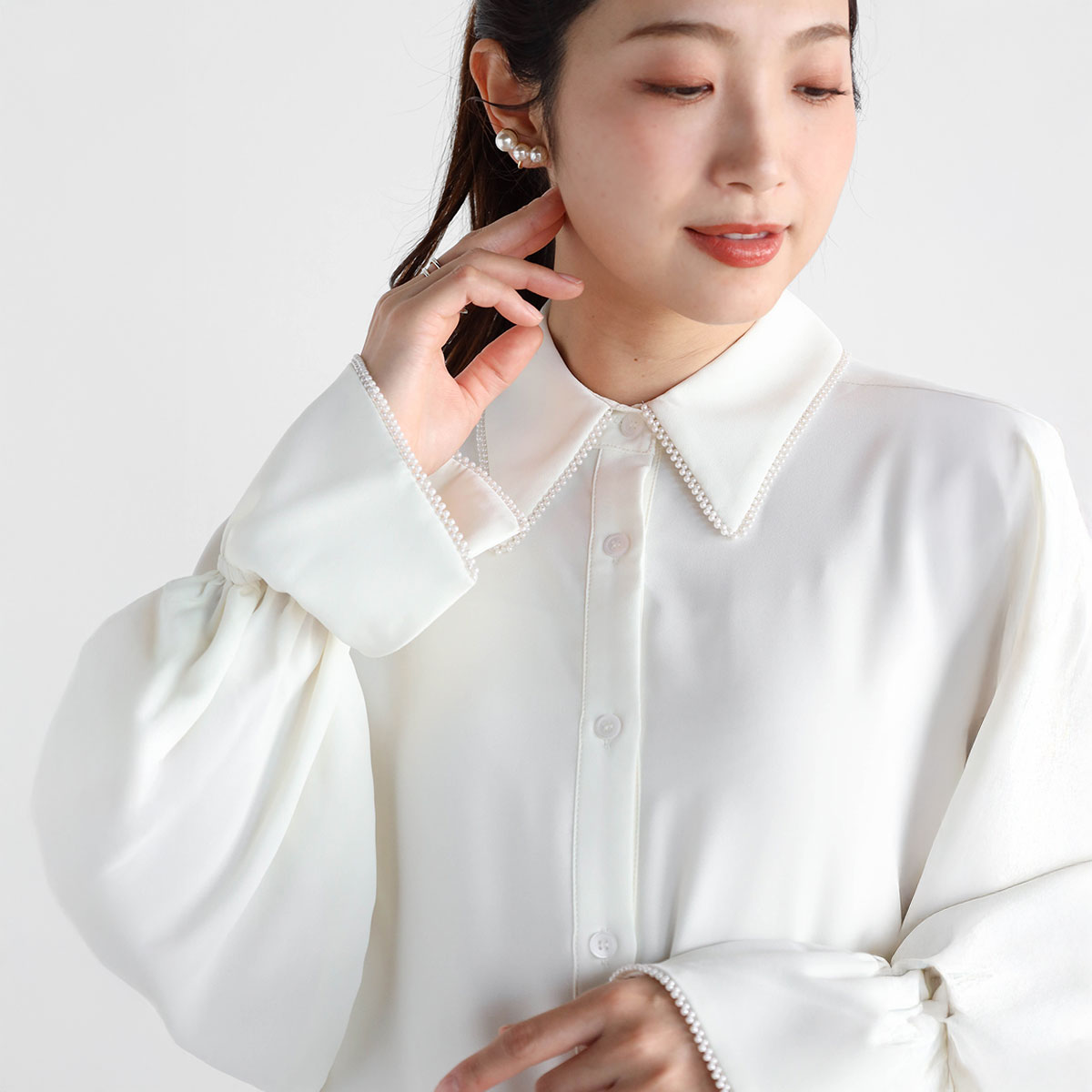 襟元と袖口にあしらったパール調の装飾が、さりげなく華やかさを添えるブラウス。 柔らかな生地感と袖のボリュームスリーブが、動くたびに女性らしさを引き立てます。 1枚で主役になる存在ながら、ジャケットやベストを重ねるのもオススメ。 デイリーから...