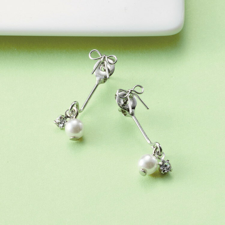 リボンモチーフが揺れるパールを組み合わせた可愛いピアス。クールなスタイルにも女性らしさを演出します。耳元で揺れるキュートなデザイン。真鍮（ロジウム色メッキ）、クリスタルガラス、人工真珠（プラスチックパール）（径約4mm）全長約2.3cm、リ...