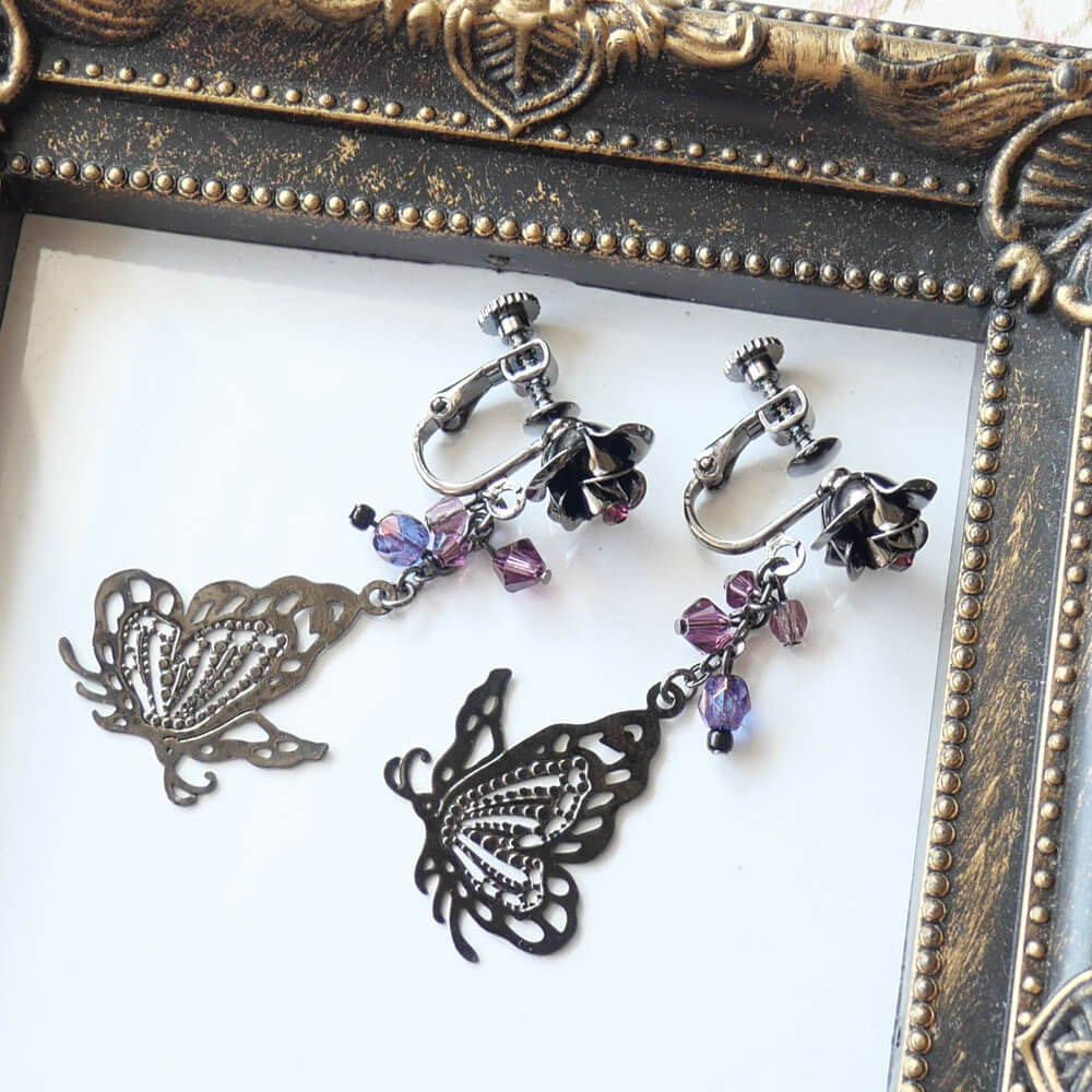 【ローズガーデン シリーズ】 パープルローズ×ガンメタバタフライのゴスロリ風イヤリング パープルストーンの薔薇の下で繊細なステンドバタフライが揺れる カットガラス、ビーズもパープル系で統一 ガンメタ仕上げ 【サイズ】 　全長　縦：約5センチ...